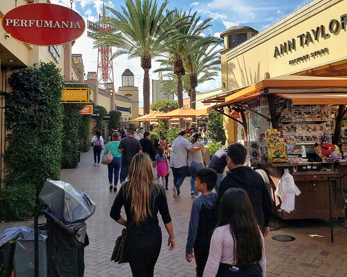 Shoppers flow through the Perfumania corridor like a river of retail enthusiasm, palm trees standing sentinel over their journey.
