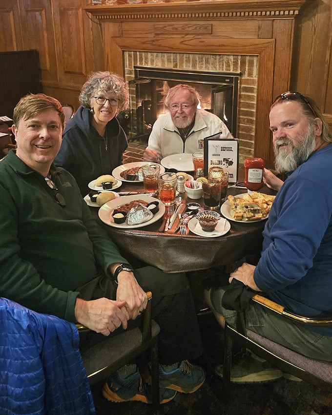 Happy diners gathered around a fireplace with loaded plates&mdash;this is what they mean by "breaking bread" in its most joyful form.