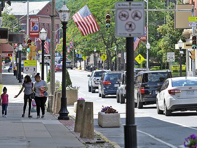 Experience the bustling energy of Fitchburg as you walk past vibrant flags, historic architecture, and friendly locals on a sunny day.