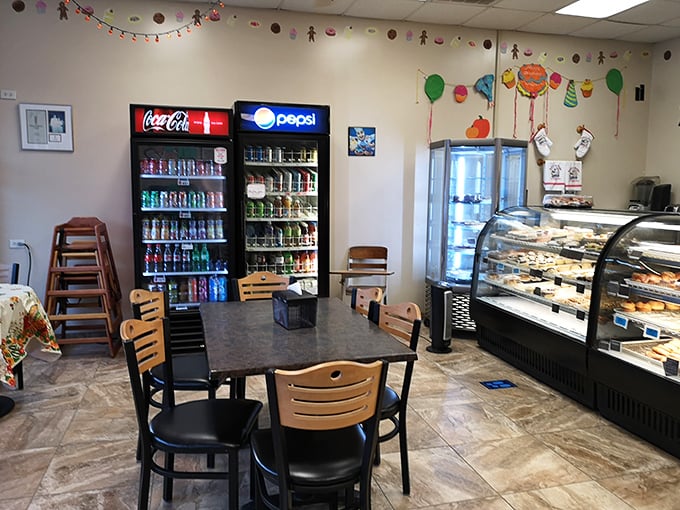 The drink coolers stand sentinel beside display cases. In the great debate of donut pairings, both Coke and Pepsi fans find common ground here.