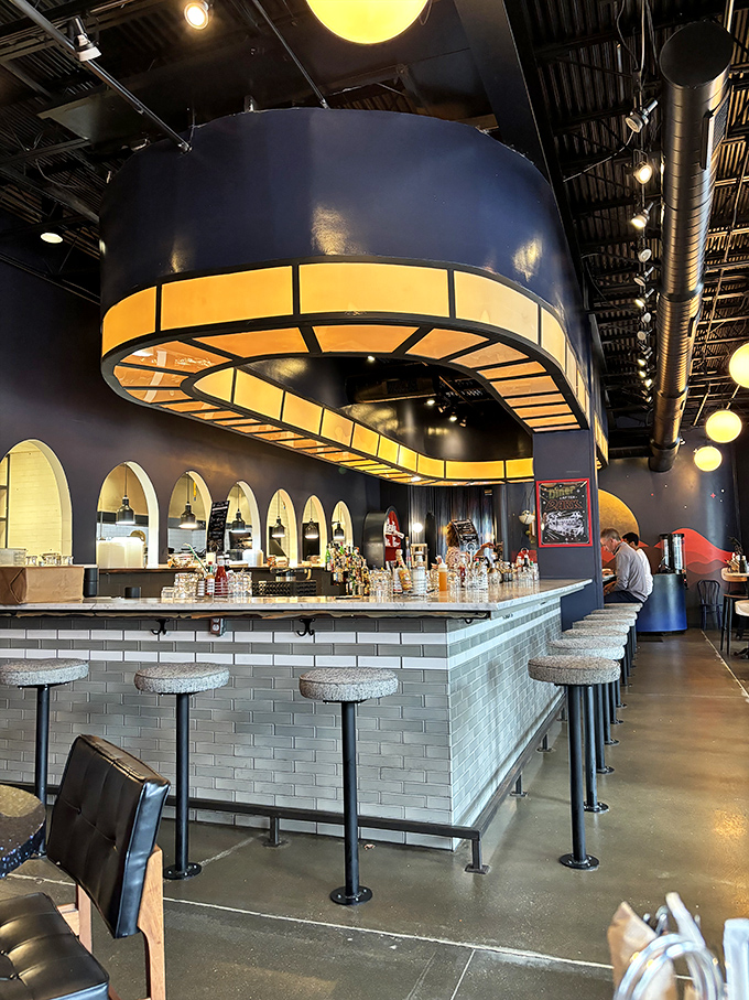 The bar area's illuminated circular fixture hovers like a friendly UFO, casting a warm glow over patrons perched on speckled stone stools.