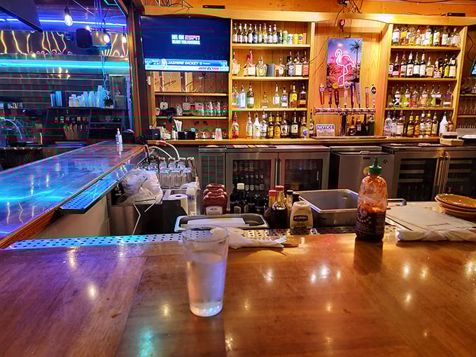 The bar isn't just stocked&mdash;it's a liquid library of possibilities where blue lights and amber bottles create a twilight atmosphere of potential.