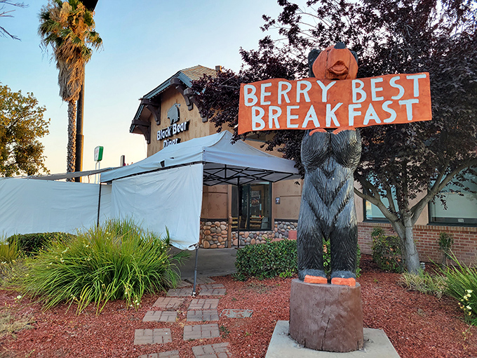 Nothing says "welcome to affordable small-town living" quite like a bear statue holding your breakfast sign with unironic enthusiasm.
