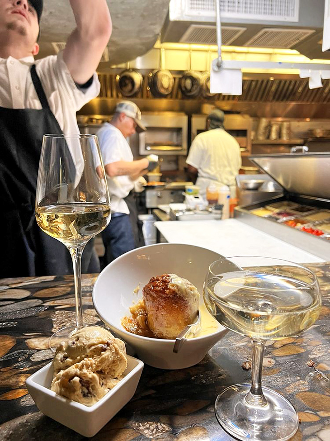 Wine glasses and small plates create the perfect tableau for culinary exploration. The open kitchen in the background promises transparency in deliciousness.