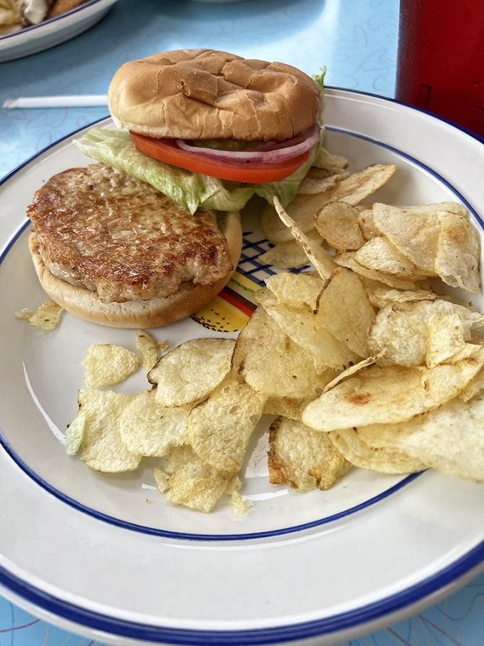 A sandwich that understands the importance of proper architecture—sturdy bun, perfectly grilled meat, fresh veggies, and those chips standing by for textural support.