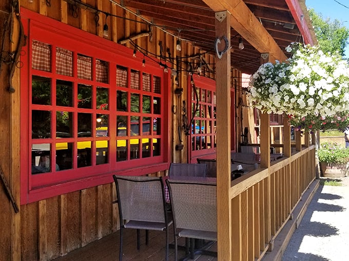 Red-trimmed windows frame the outdoor seating area, where hanging flowers and wooden railings create a charming frontier vibe.