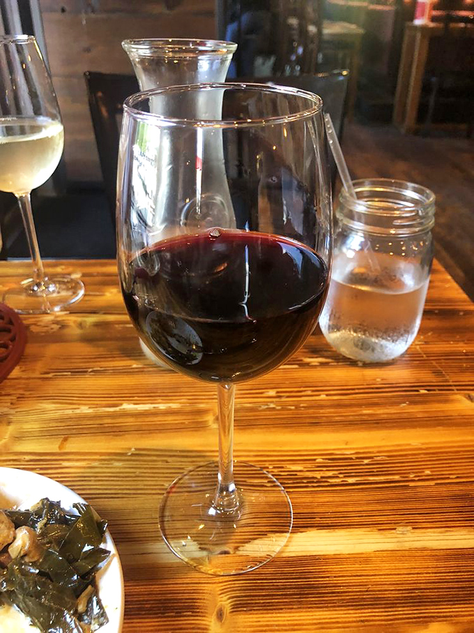 A glass of red wine catching the light just right – because sometimes civilization is exactly what you need with Southern comfort food.