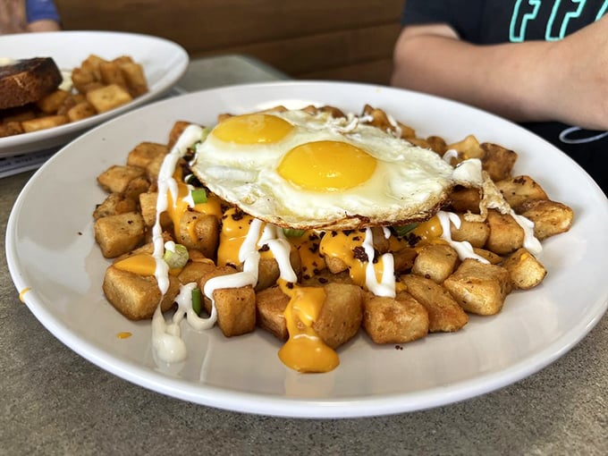 Breakfast architecture at its finest: perfectly fried eggs crowning a mountain of seasoned potatoes drizzled with twin sauces like a morning masterpiece.