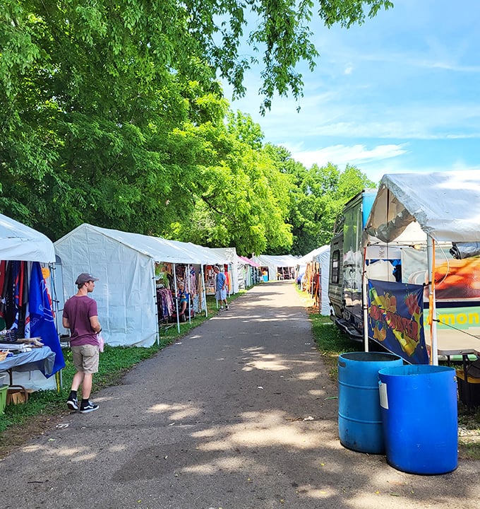 White tents create a temporary neighborhood of commerce under leafy green canopies. The pathway practically whispers, "Who knows what you'll discover around the next corner?"