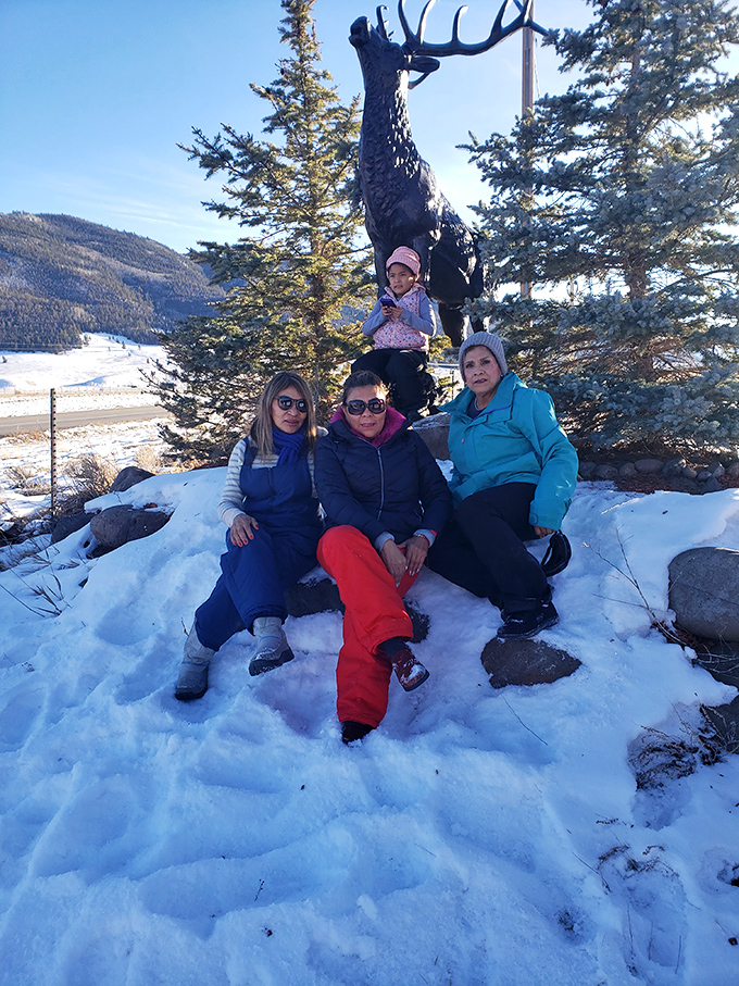 A winter scene that reminds us some memories are best made against a backdrop of snow, mountains, and a large metal elk statue.
