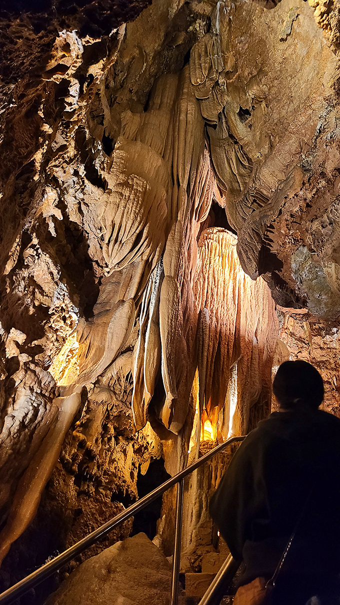 These flowing stone curtains look ready to part for Earth's greatest show. A visitor silhouetted against nature's grandeur provides perfect scale for this underground wonder.