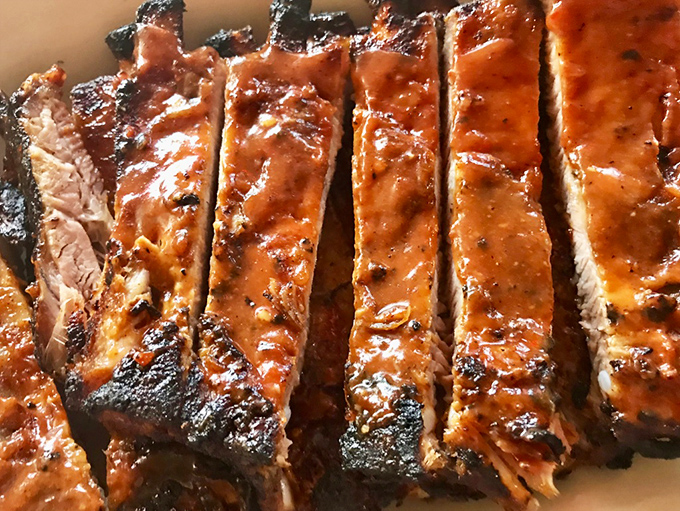 Ribs sliced with surgical precision, revealing that perfect pink smoke ring that separates barbecue artists from mere mortals with grills.