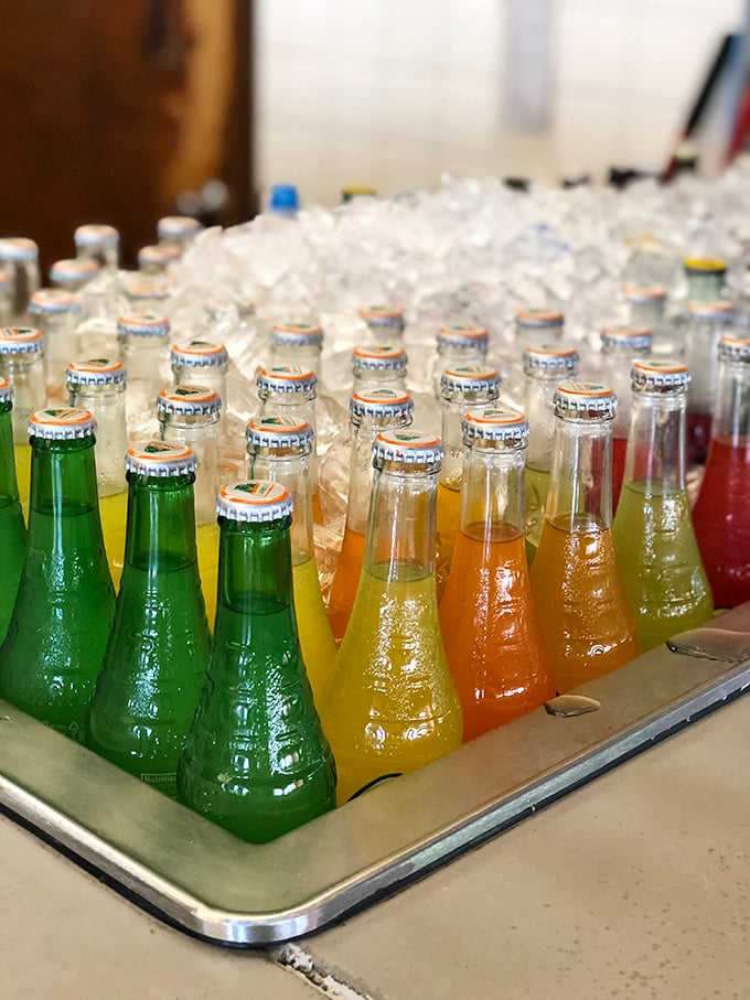 A rainbow of Mexican sodas chilling on ice – liquid jewels in glass bottles that promise exotic flavors beyond your standard cola experience.