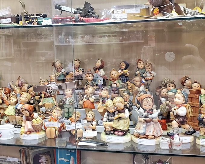 A glass menagerie of Hummel-style figurines stands at attention, their rosy cheeks and innocent expressions unchanged since they first graced grandmothers' curio cabinets.
