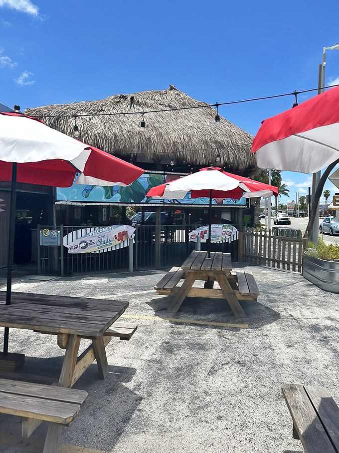 Red and white umbrellas shade wooden picnic tables on a sandy patch&mdash;because sometimes the best seafood comes with a side of Florida sunshine.