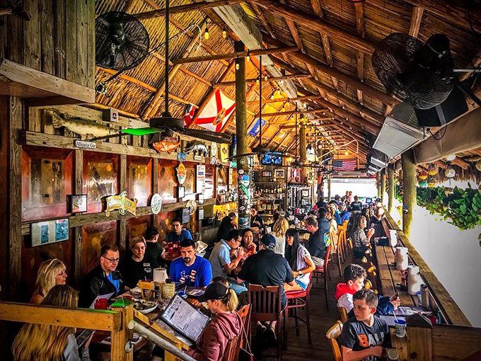 The tiki bar's vaulted thatch ceiling creates a cathedral of casual dining where seafood worship happens daily among the faithful