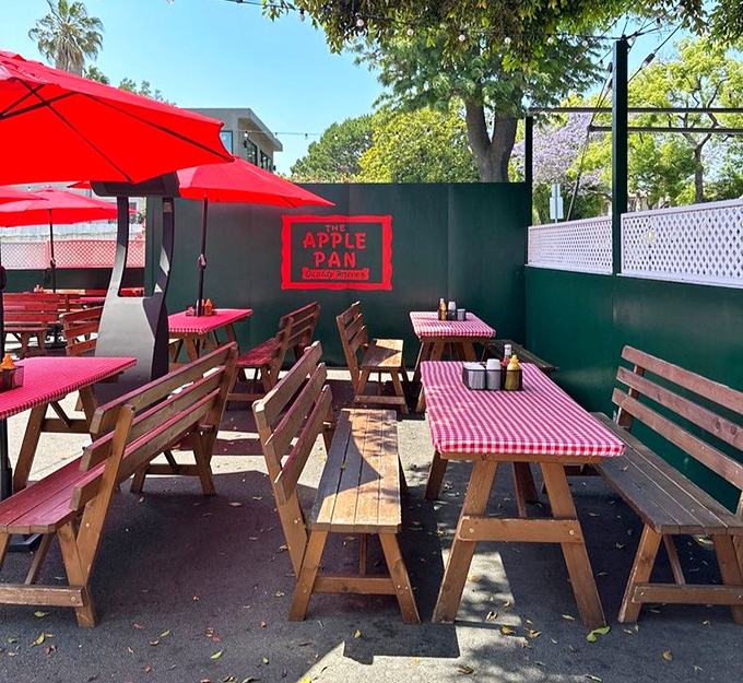 The outdoor patio area offers a more modern touch with its picnic tables and red umbrellas, though purists might argue the true Apple Pan experience happens only at the counter.