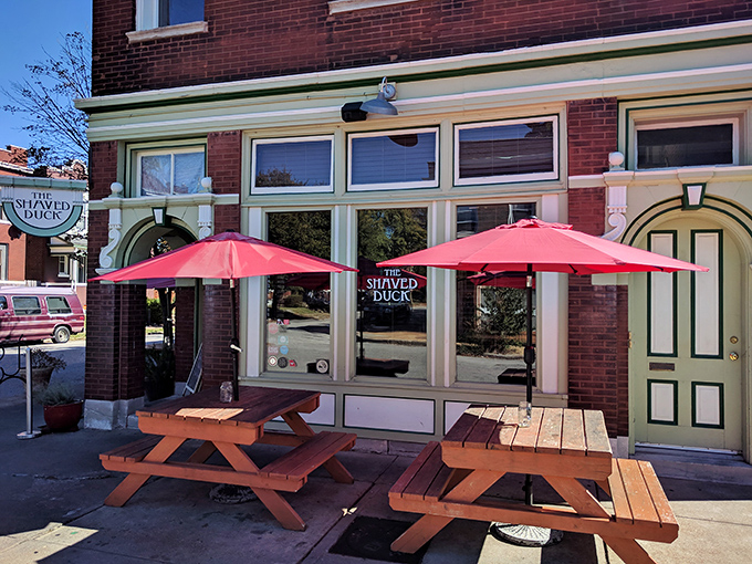 Red umbrellas and wooden picnic tables create a sidewalk oasis where summer afternoons stretch lazily into evening feasts.