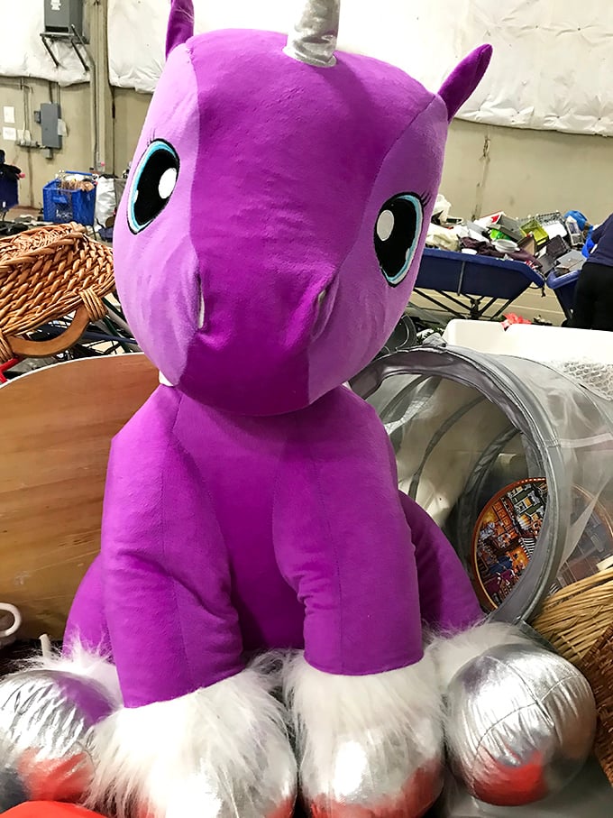 A purple unicorn plushie surveys the chaos with wide-eyed optimism, ready for a second chance at bringing joy to a new home. 