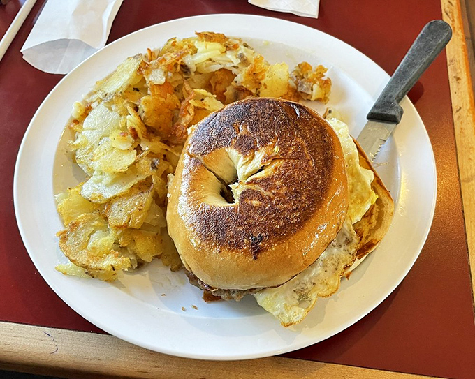 Breakfast architecture at its finest: a toasted bagel sandwich stacked with eggs and protein, with home fries standing guard on the perimeter.