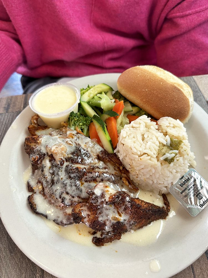 Blackened fish draped in creamy sauce alongside perfectly formed rice and fresh vegetables &ndash; a plate that balances indulgence with virtue.