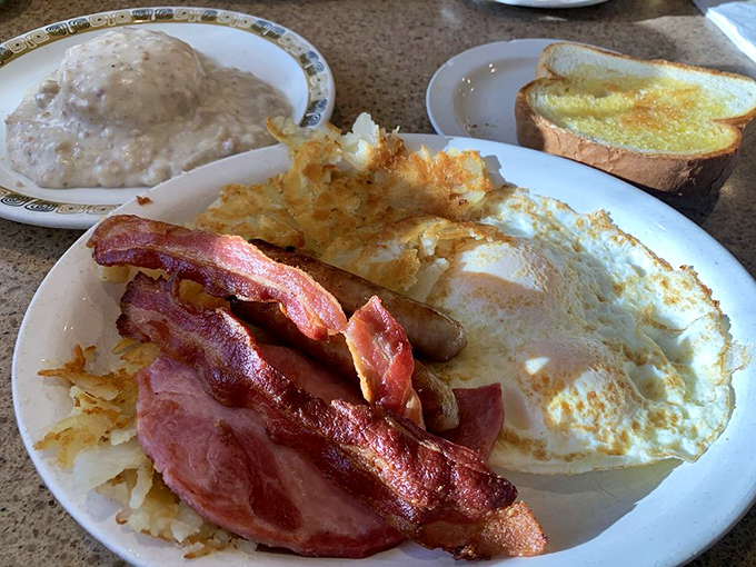 Breakfast harmony achieved: crispy-edged eggs, bacon with that perfect bend, hash browns with golden crowns, and toast waiting patiently for its butter to melt.