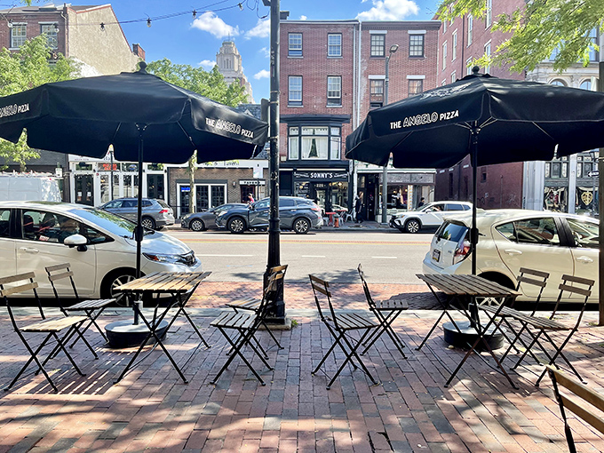 Sidewalk seating under black umbrellas, where lucky diners savor their prizes. A quintessential Philadelphia street scene with the city's architecture creating the perfect backdrop.