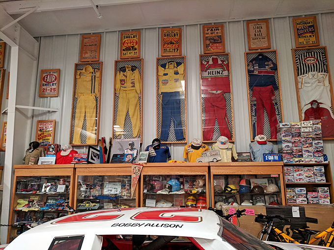 Racing suits hang like colorful banners of glory, each representing a driver who risked everything for the checkered flag and immortality.