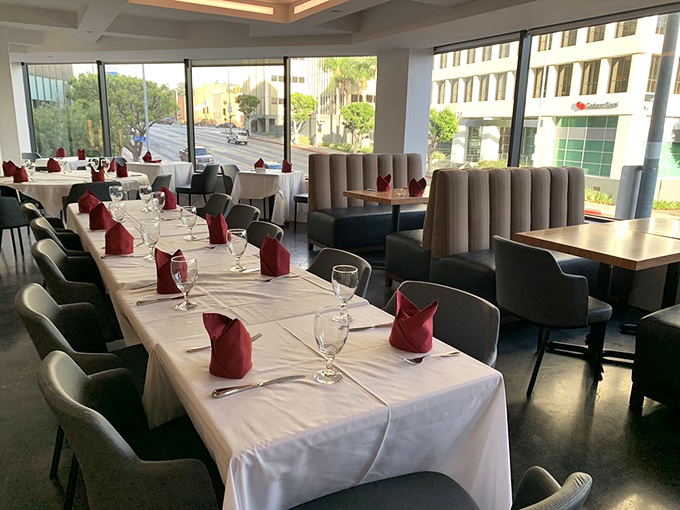 Floor-to-ceiling windows flood the space with natural light, making those burgundy napkins pop like rubies on a white canvas.