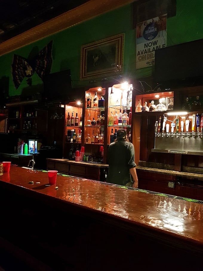 The bar gleams with promise in the dim light, bottles standing at attention like soldiers ready to serve in the battle against sobriety.