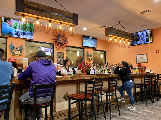 The bar area balances rustic wooden elements with vibrant orange walls, creating the perfect backdrop for margarita-fueled conversations and laughter.