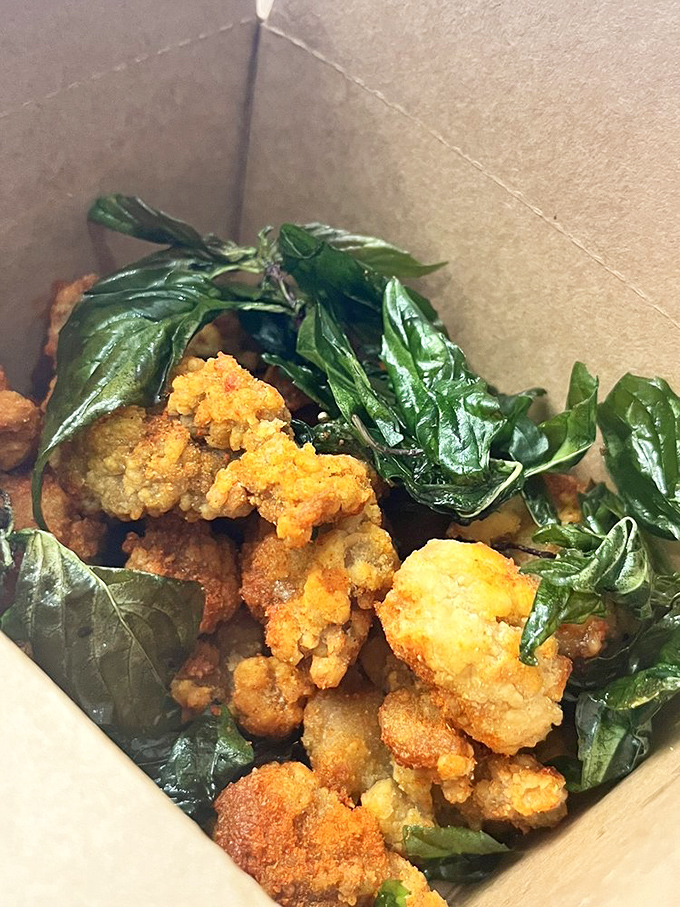 Crispy chicken nestled with fresh basil leaves in a cardboard cradle&mdash;street food elevated to an art form without losing its soul.