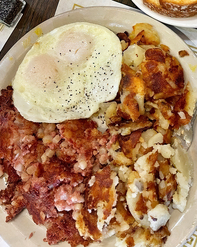 A breakfast trinity: perfectly cooked egg, crispy corned beef hash, and golden potatoes &ndash; simple ingredients elevated through proper cooking technique.