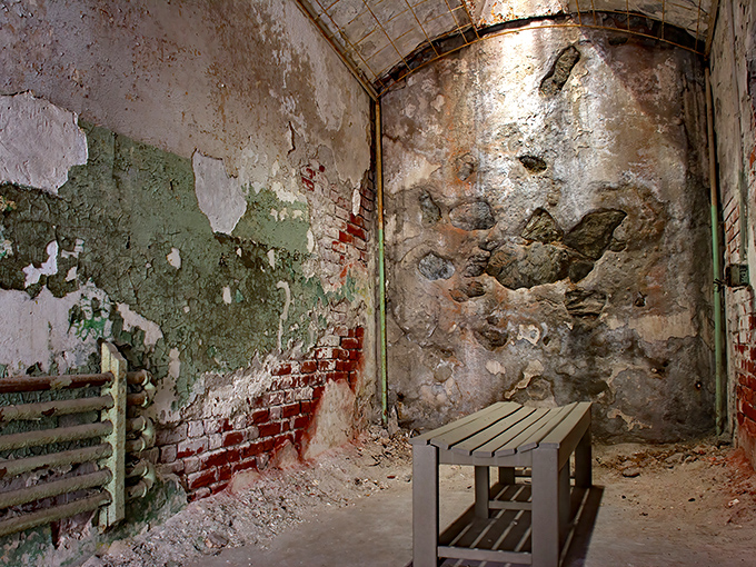 Peeling paint and crumbling walls create an eerie atmosphere in this empty cell. The ghosts of conversations past seem to echo off the walls.