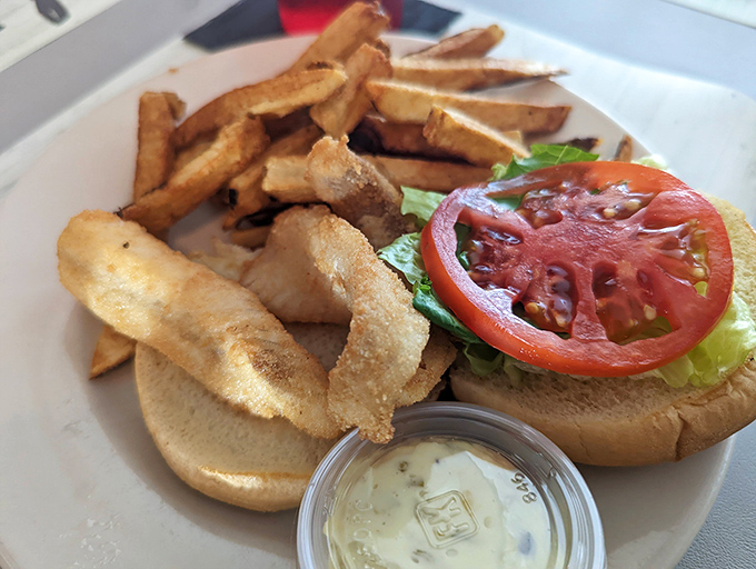 A sandwich that understands the importance of proper architecture—sturdy bun foundation, strategic tomato placement, and crispy fish as the centerpiece.