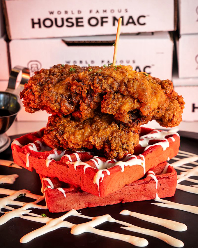 Fried chicken perched atop red velvet waffles like royalty on a crimson throne, waiting for its syrup coronation.