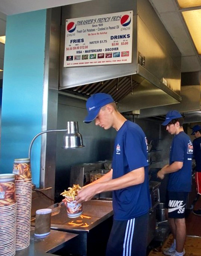 The blue-uniformed fry technicians move with practiced precision, having mastered the delicate art of potato-to-oil-to-cup choreography.