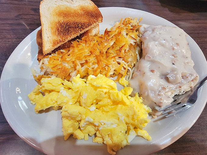 The holy trinity of breakfast comfort&mdash;golden hashbrowns, fluffy scrambled eggs, and biscuits swimming in creamy gravy. Grandma would approve, then ask for seconds.