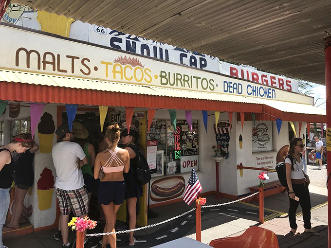 The Snow Cap's exterior welcomes hungry travelers with its "MALTS, TACOS, BURRITOS, DEAD CHICKEN" promise &ndash; a menu that's both appetizing and amusing.