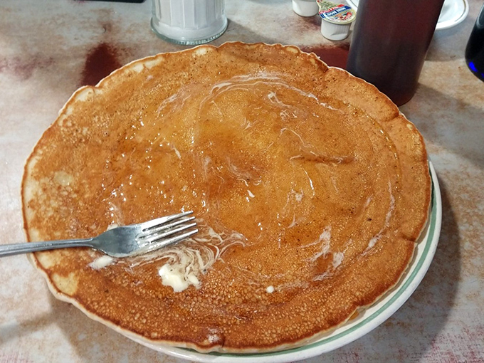 This isn't just a pancake—it's a plate-sized canvas of golden-brown perfection waiting for its maple syrup waterfall moment.