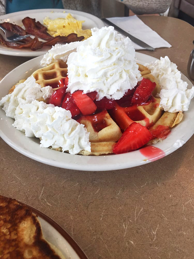 Not just a waffle—a throne for strawberry royalty, crowned with whipped cream clouds so light they might float away if not for the sweet anchor below.