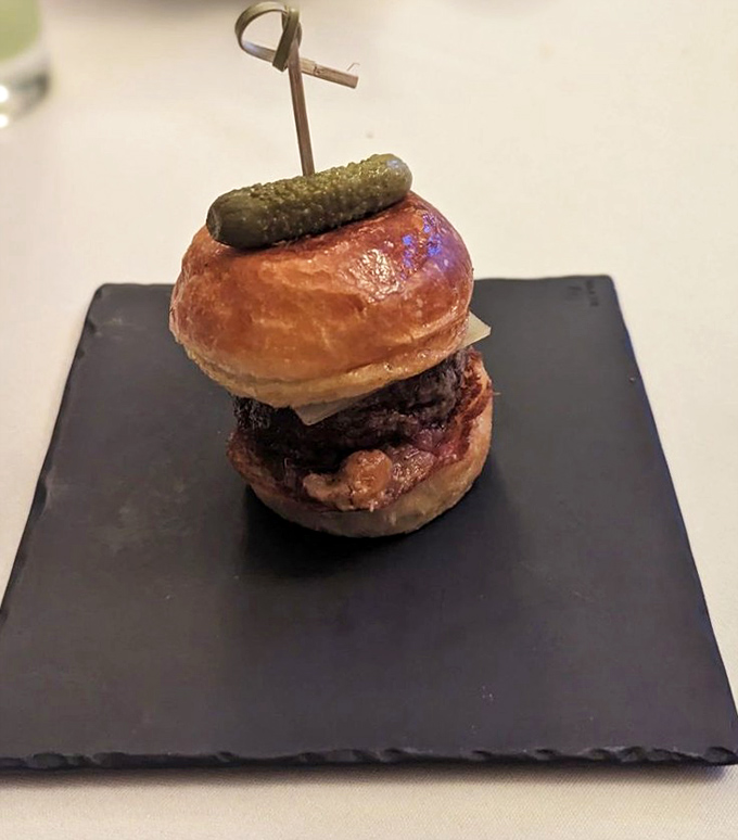 This isn't just a slider; it's a tiny tower of beef perfection topped with a pickle crown. Royalty in miniature form.