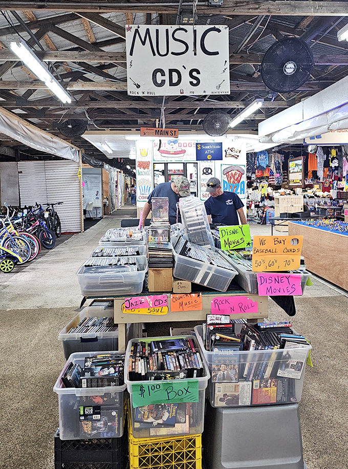 Music archeology in action! Vinyl records and CDs organized in plastic bins, where nostalgic shoppers dig for forgotten soundtrack treasures from better decades.