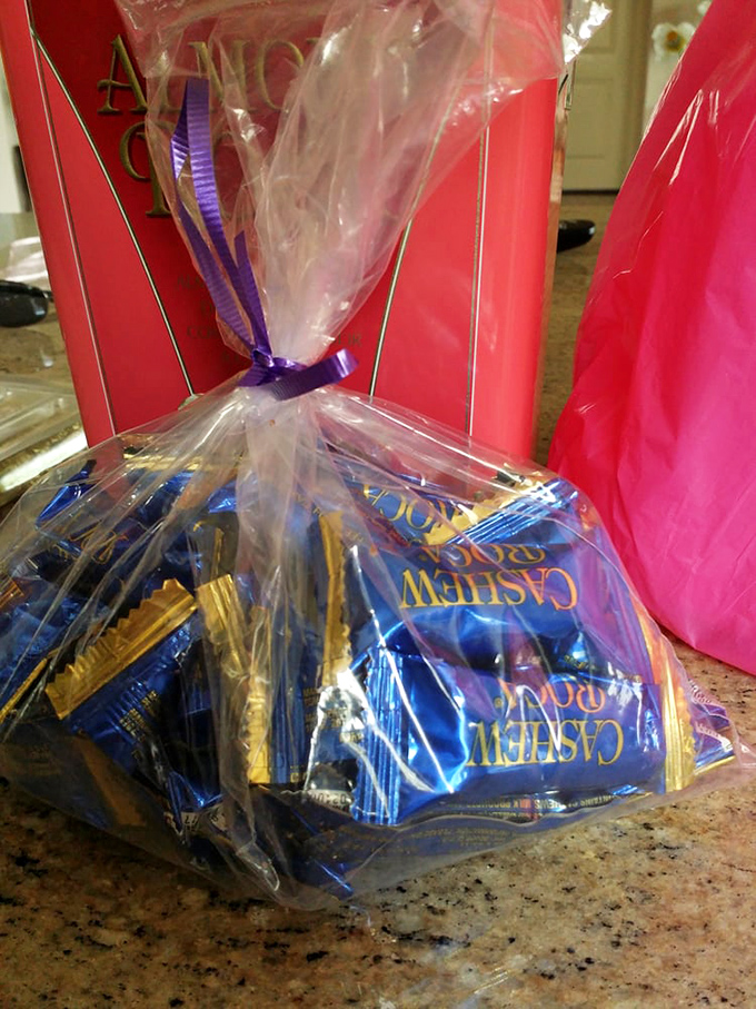 Gift bags of Cashew Roca tied with purple ribbon &ndash; because sometimes saying "I care about you" requires chocolate ammunition.