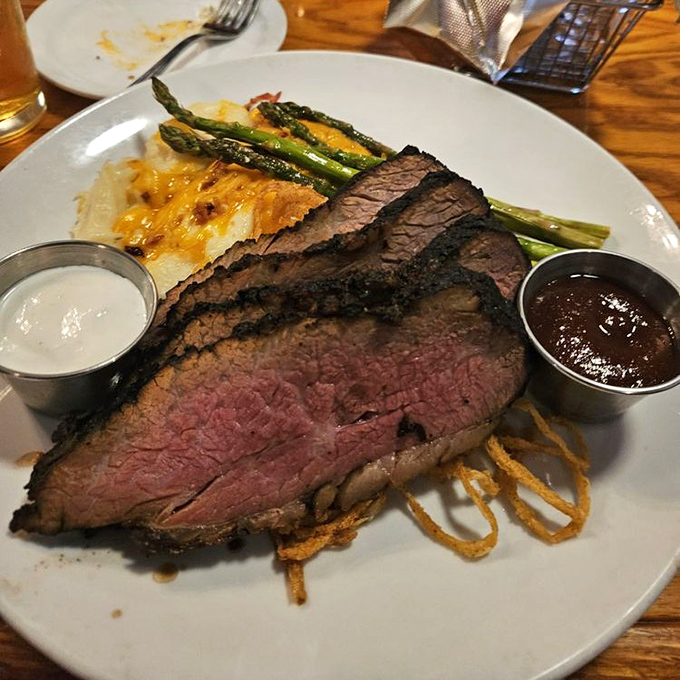 Tri-tip sliced to showcase its perfect medium-rare interior, flanked by asparagus spears and sauces that enhance without overwhelming.