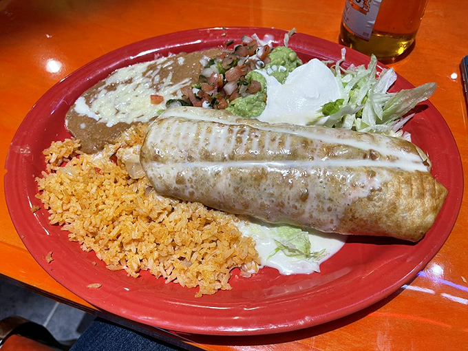 The chimichanga arrives like a sleeping giant on a red plate, surrounded by the classic rice-beans-lettuce trio that never disappoints.