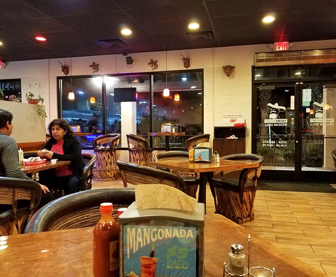 The dining room buzzes with satisfied customers, hot sauce bottles standing guard. That Mangonada sign promises refreshment after your spice adventure.