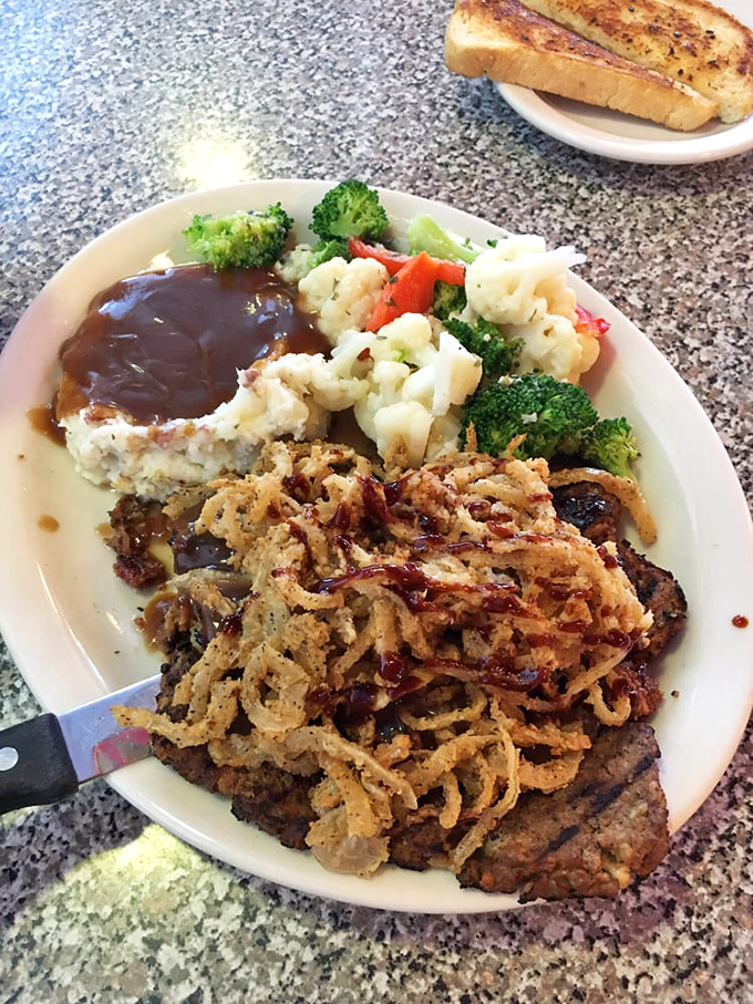 Meatloaf dinner done right: savory slices topped with crispy onions alongside mashed potatoes with gravy lakes and vegetables that actually taste good.