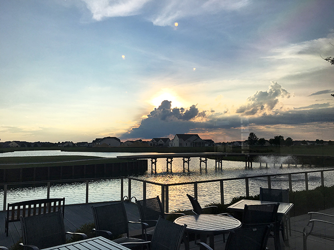 Sunset transforms the community pond into liquid gold, while patio furniture waits patiently for tomorrow's conversations and coffee.