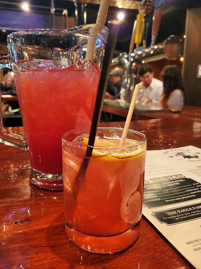 Craft cocktails glowing like liquid amber in the bar's warm light. These aren't just drinks&mdash;they're liquid courage for ordering that second helping.